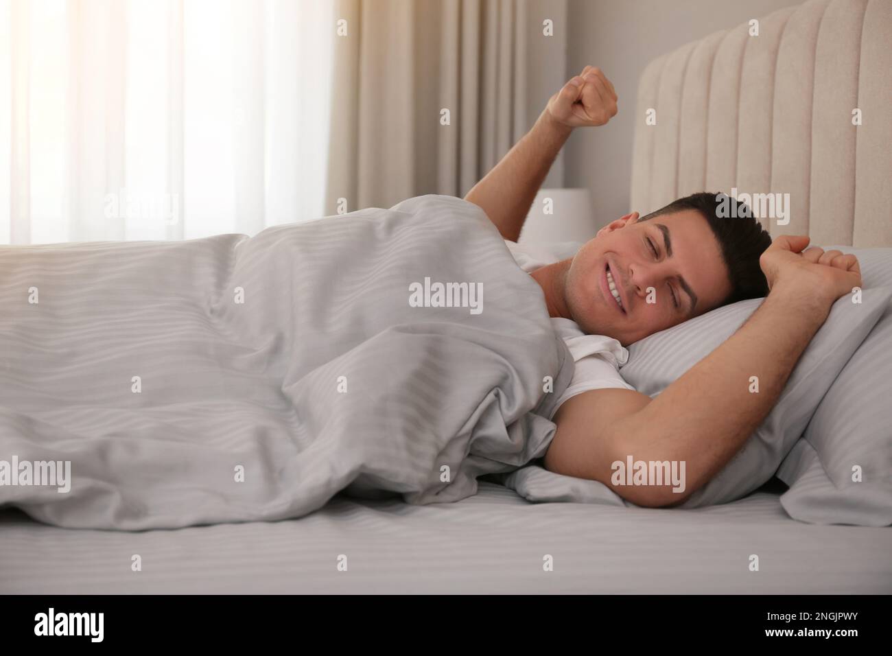 Man stretching in bed with grey linens at home Stock Photo - Alamy