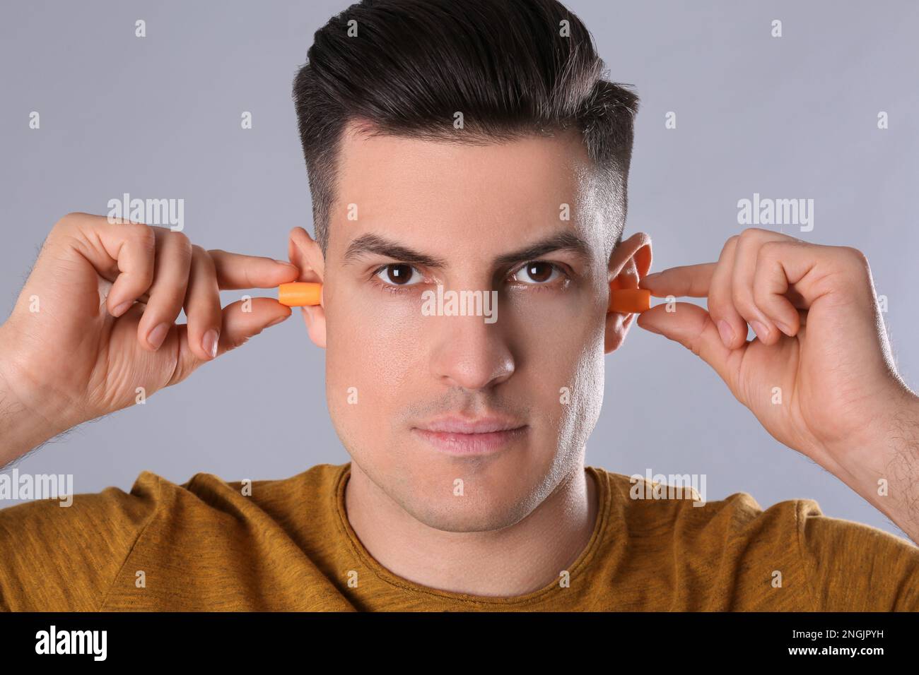 Man inserting foam ear plugs on grey background Stock Photo - Alamy