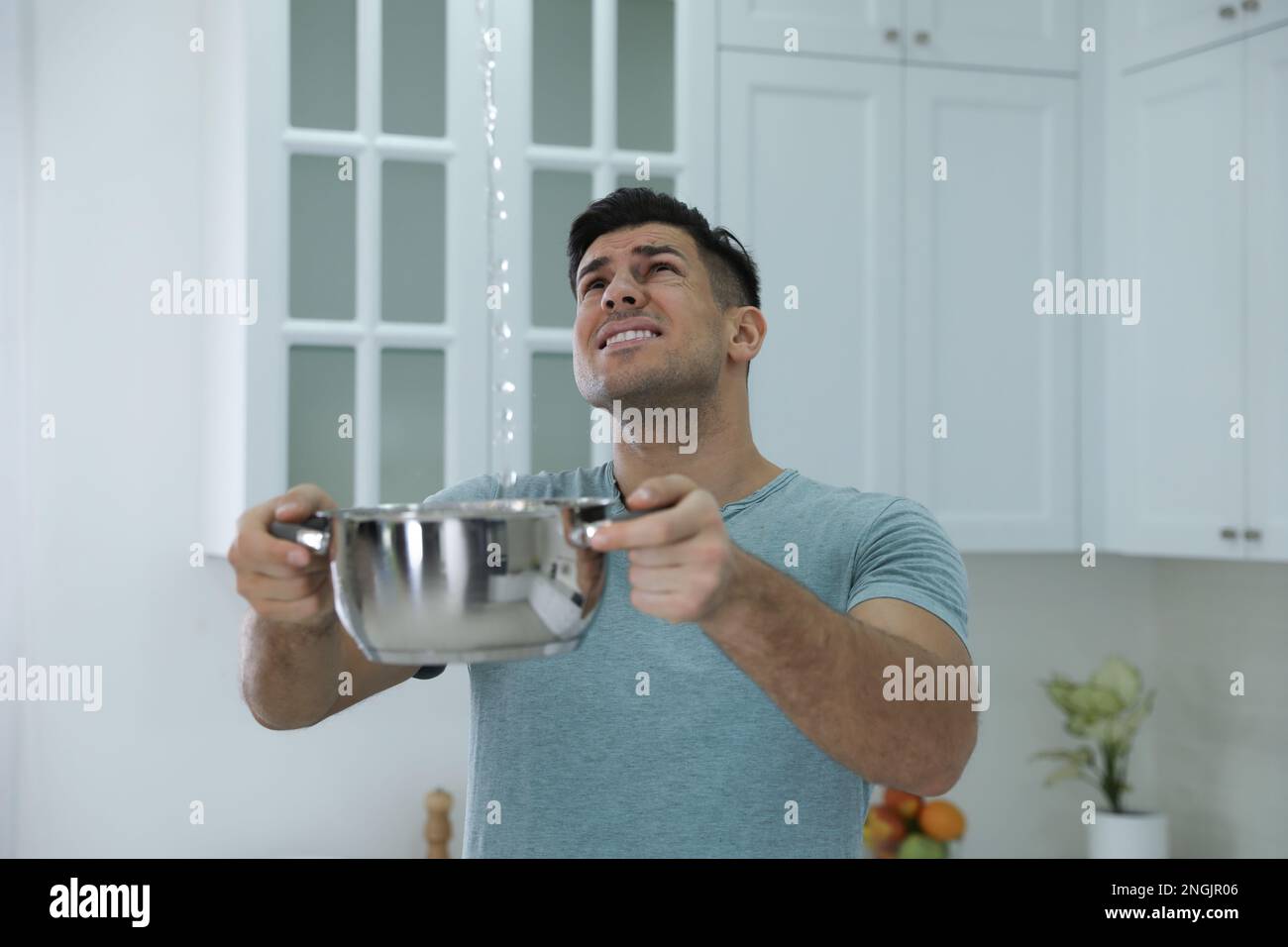 Emotional man collecting water leaking from ceiling in kitchen. Damaged ...