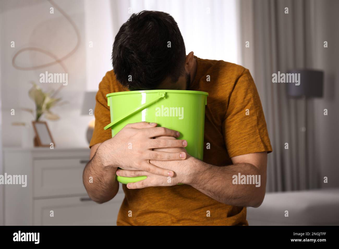 Young man with bucket suffering from nausea at home. Food poisoning ...