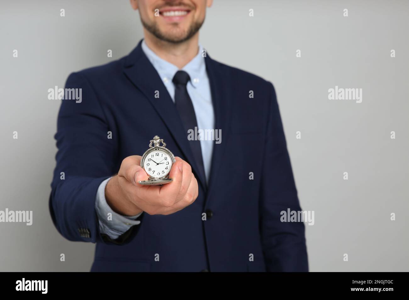 Happy businessman holding pocket watch on grey background, closeup ...