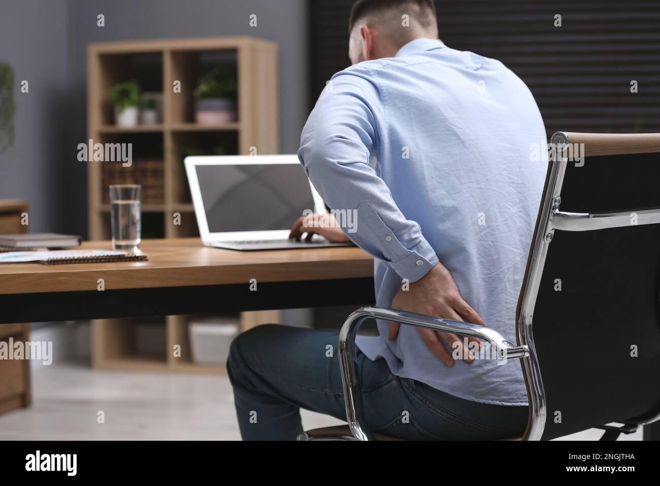 Man suffering from back pain while working with laptop in office ...