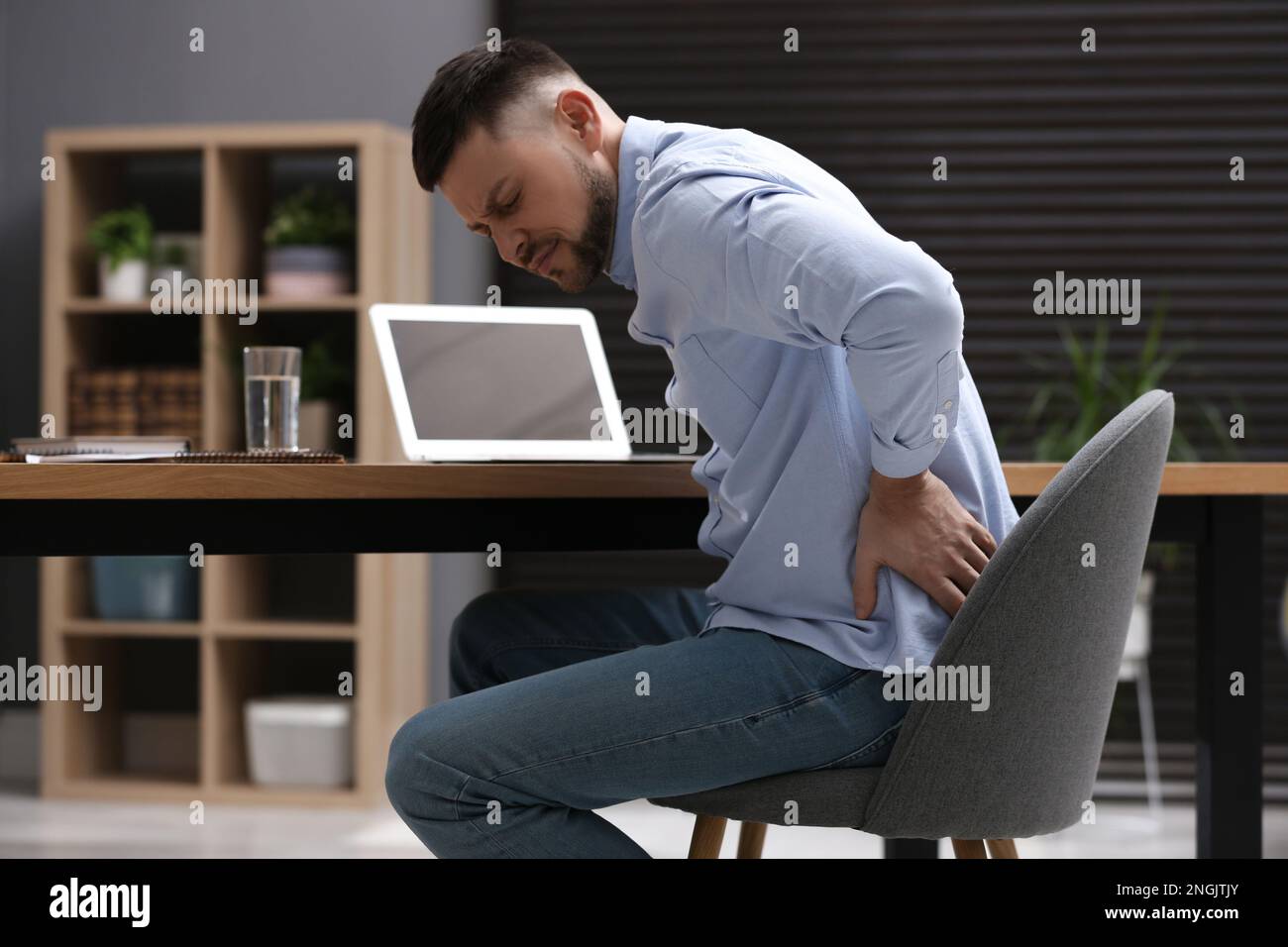 Man suffering from back pain while working with laptop in office ...