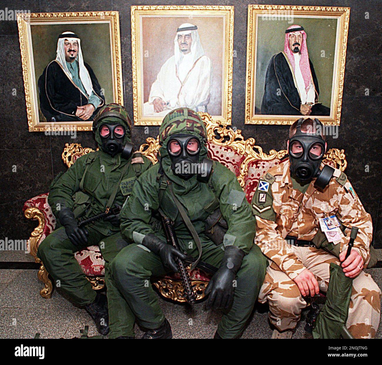 Three British soldiers, wearing chemical and biological protective gear, sit in front of ...