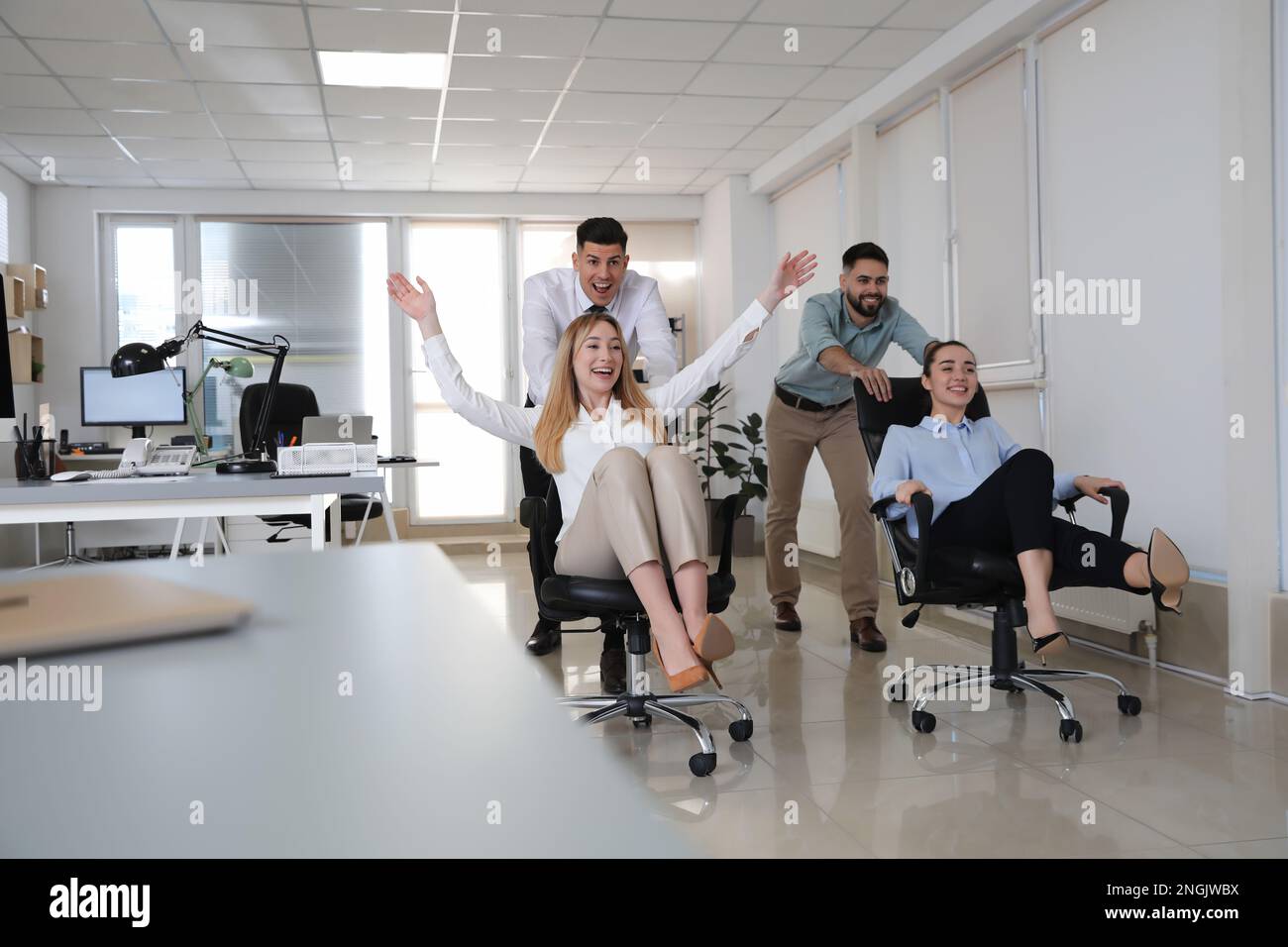 Happy office employees riding chairs at workplace Stock Photo - Alamy