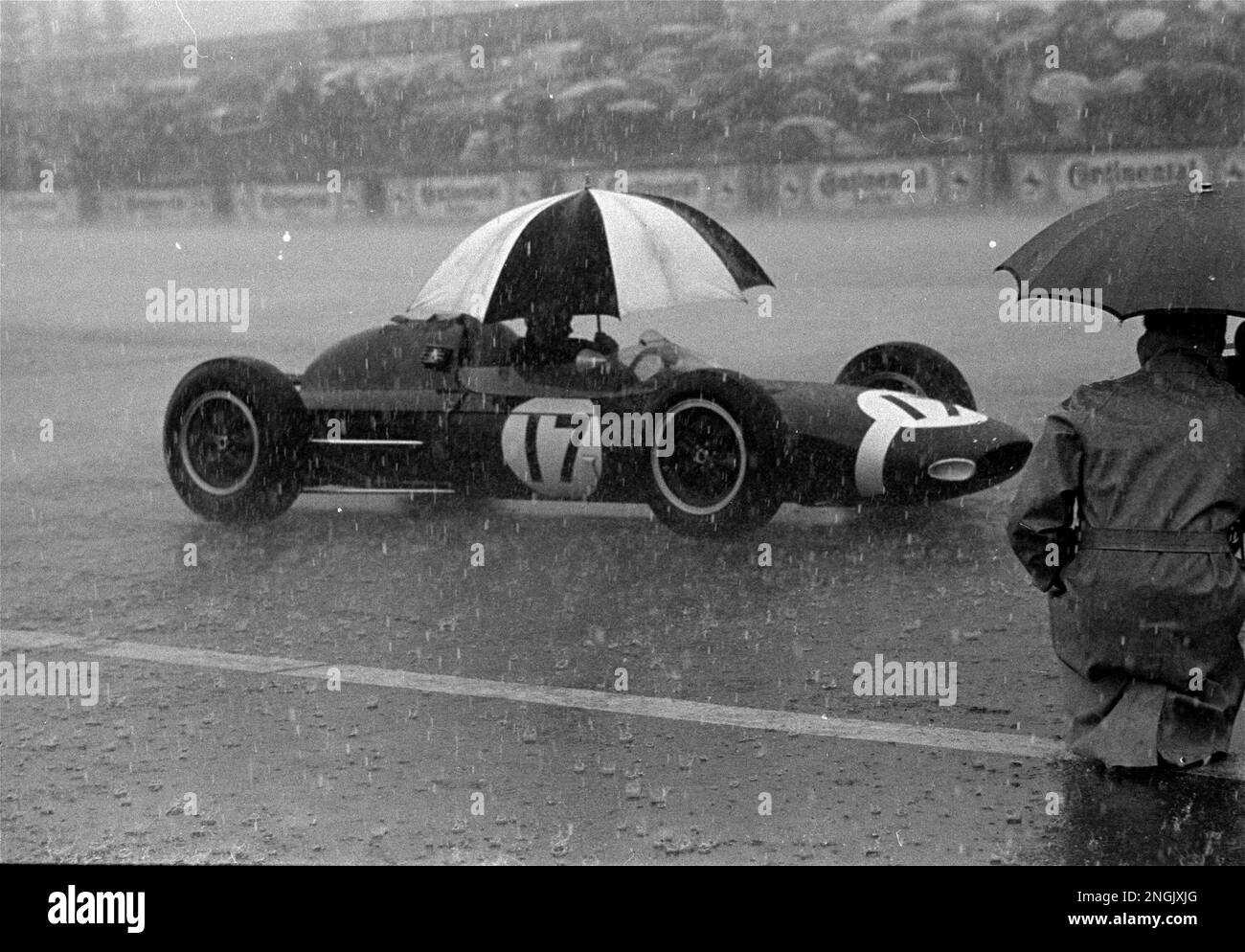 French racing driver Maurice Trintignant keeps dry under a large ...
