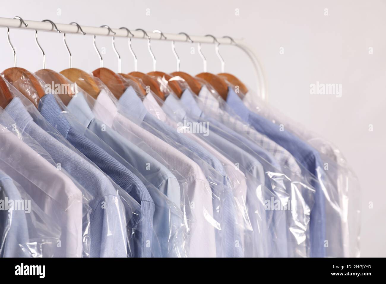Hangers with shirts in dry cleaning plastic bags on rack against light ...