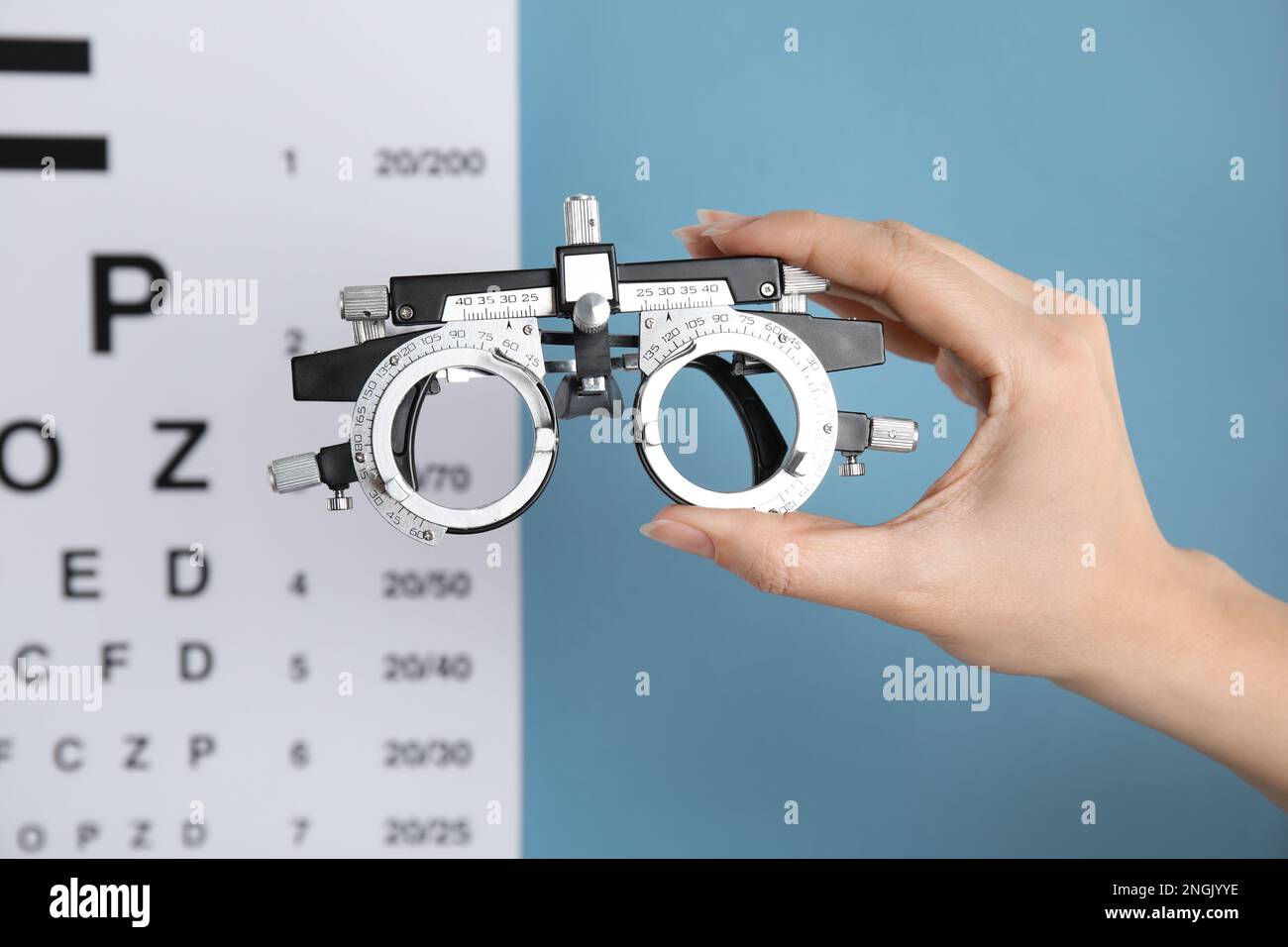 Woman holding trial frame against eye chart test on blue background ...