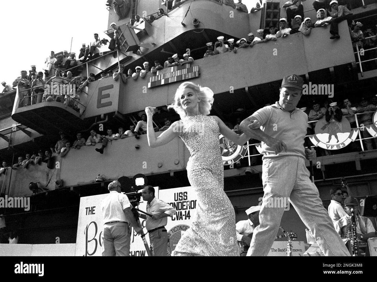 Actress Carroll Baker snaps her fingers at sailors cheering from bridge ...