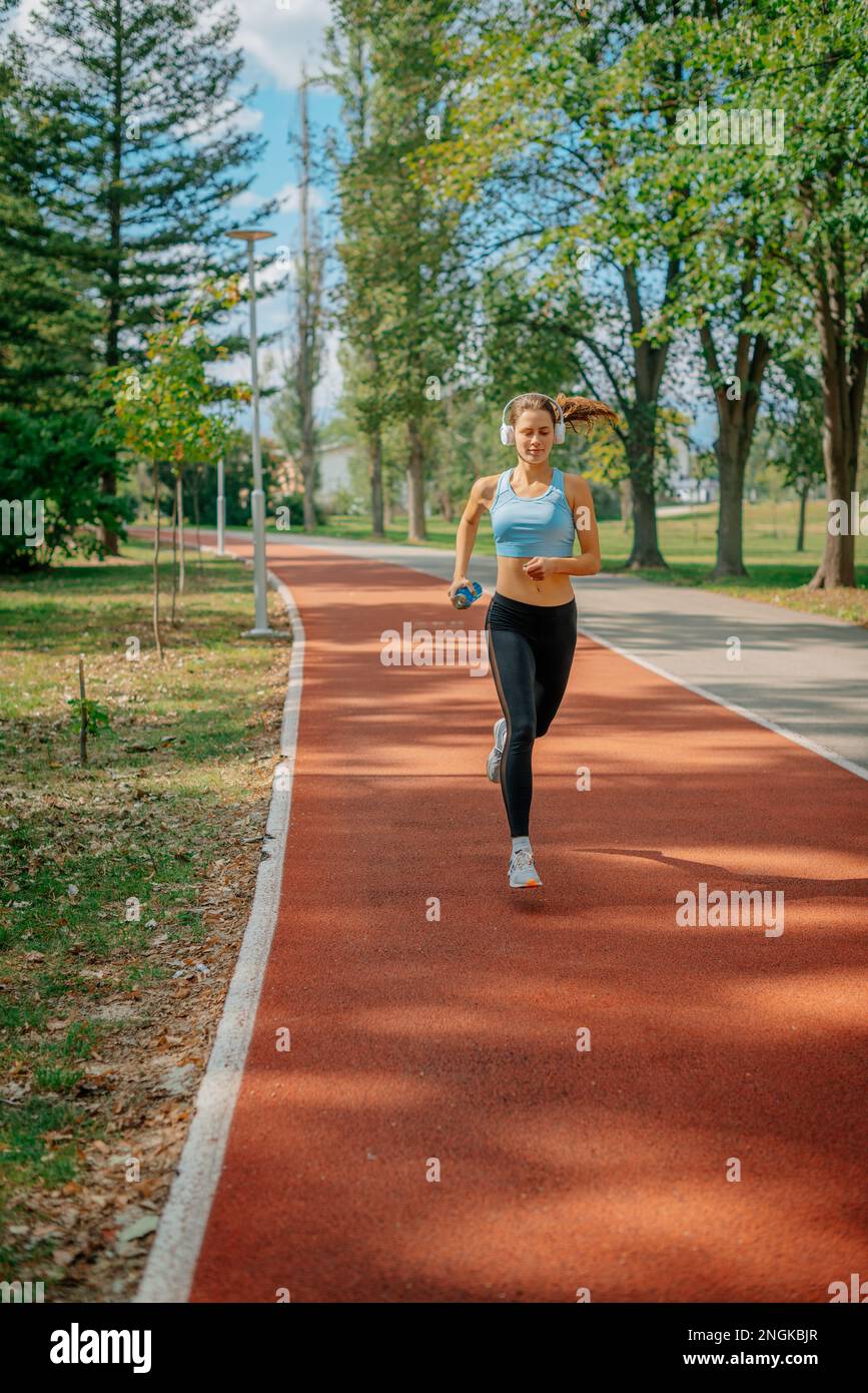 Cute young girl running on a sports track in the city park, with ...