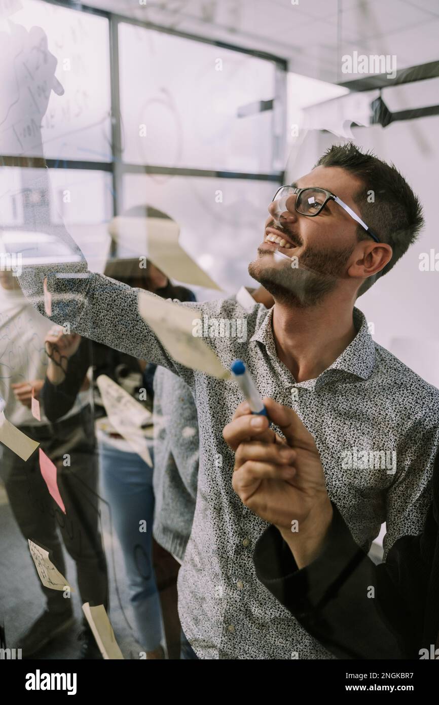 A handsome smiley male person writing over glass wall with his ...