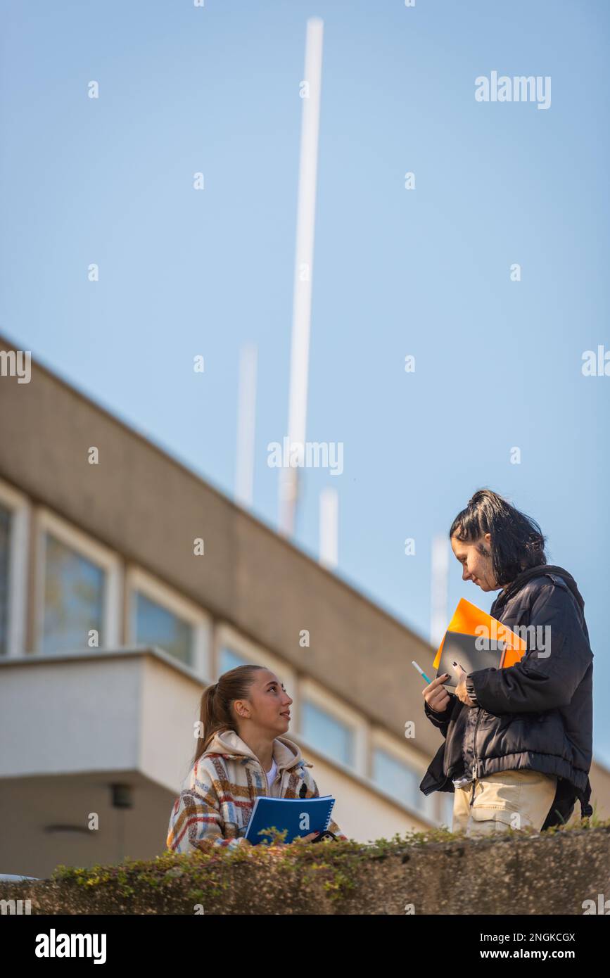 Two beautiful students talking in the school's yard. One is sitting on ...