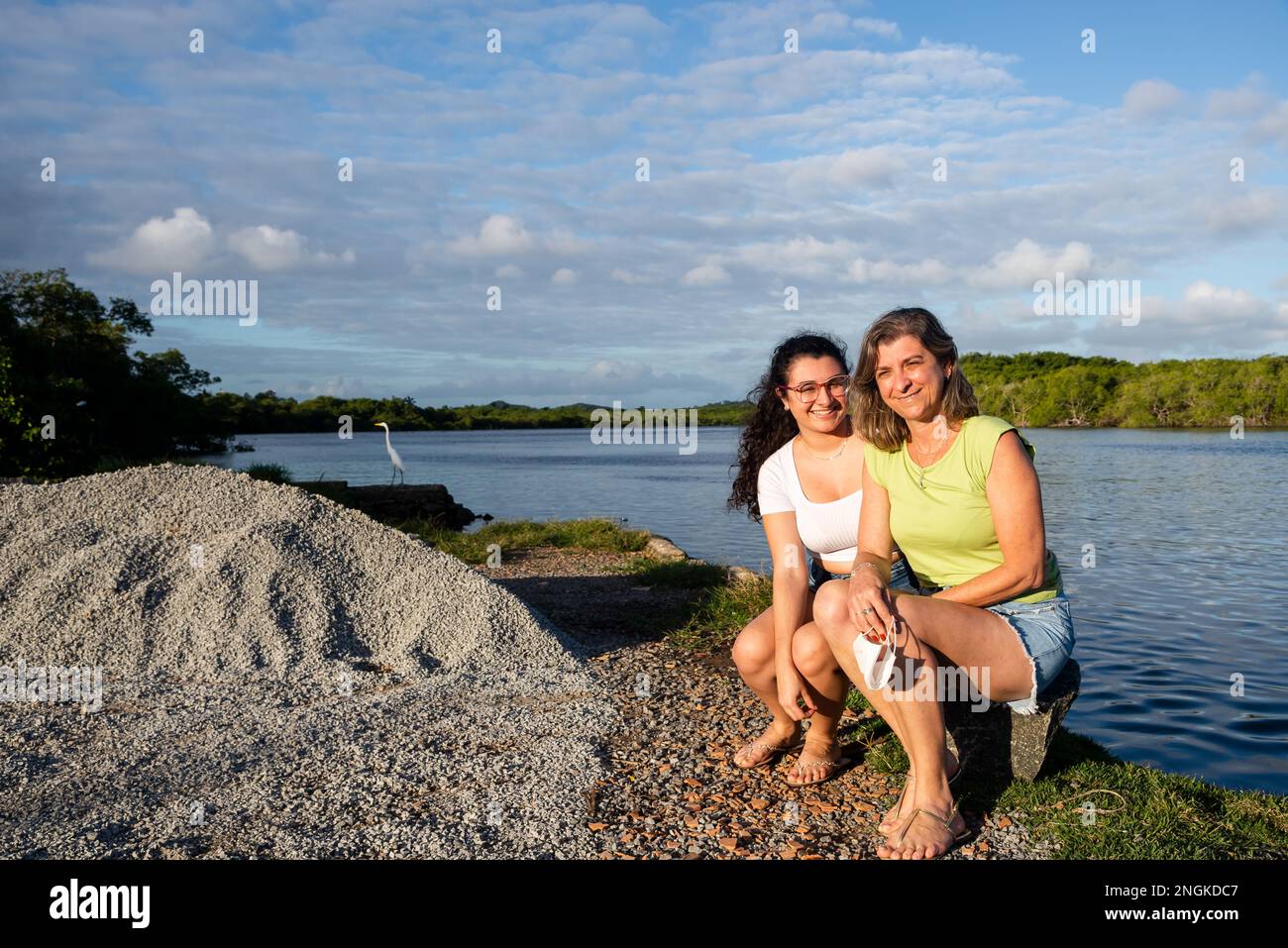 Mother and daughter sitting by the river embracing. Late afternoon ...
