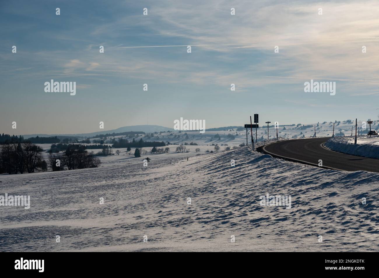 Lonely country road in winter with snow, bright sun, trees and blue sky ...