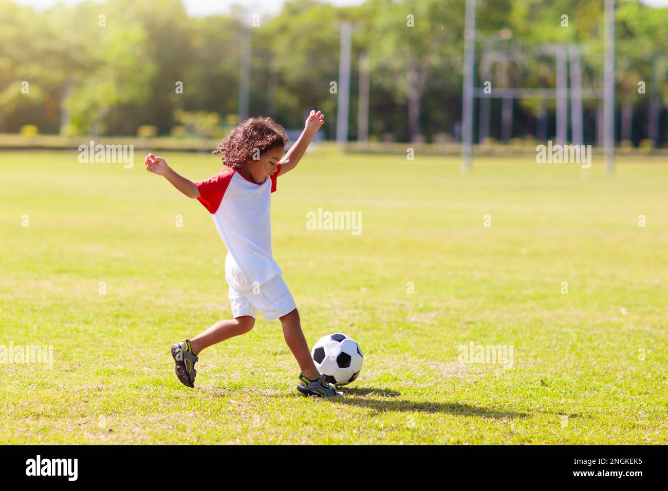 Cute curly little boy playing football. Kids play on outdoor pitch ...