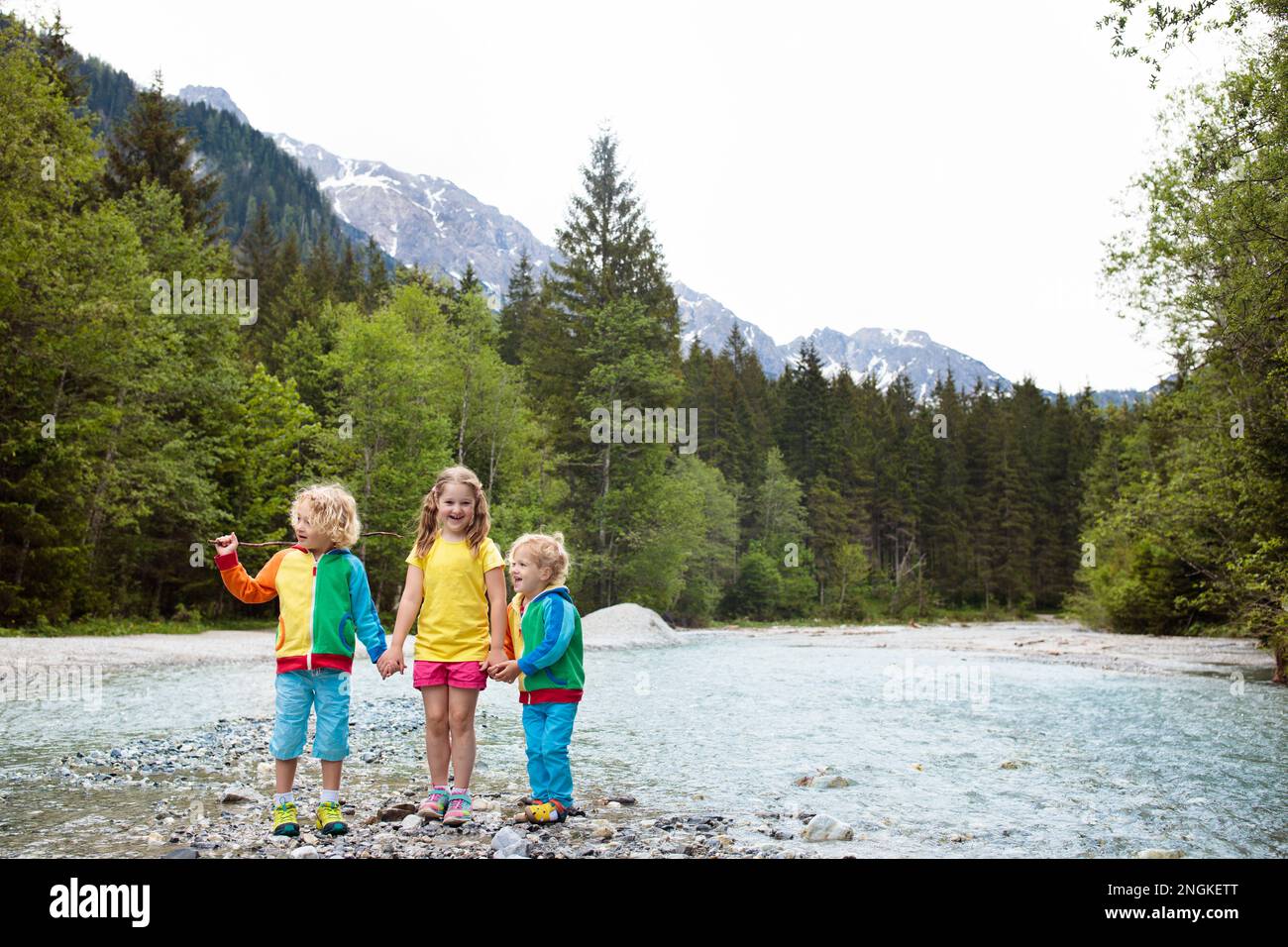 Children hiking in Alps mountains crossing river. Kids play in water at ...
