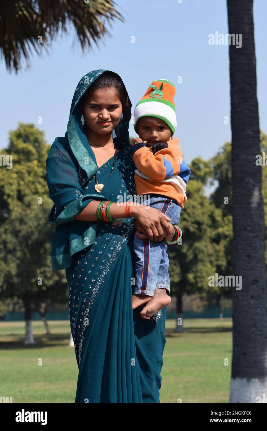 A young Indian mother dressed in a traditional sari holding her young ...