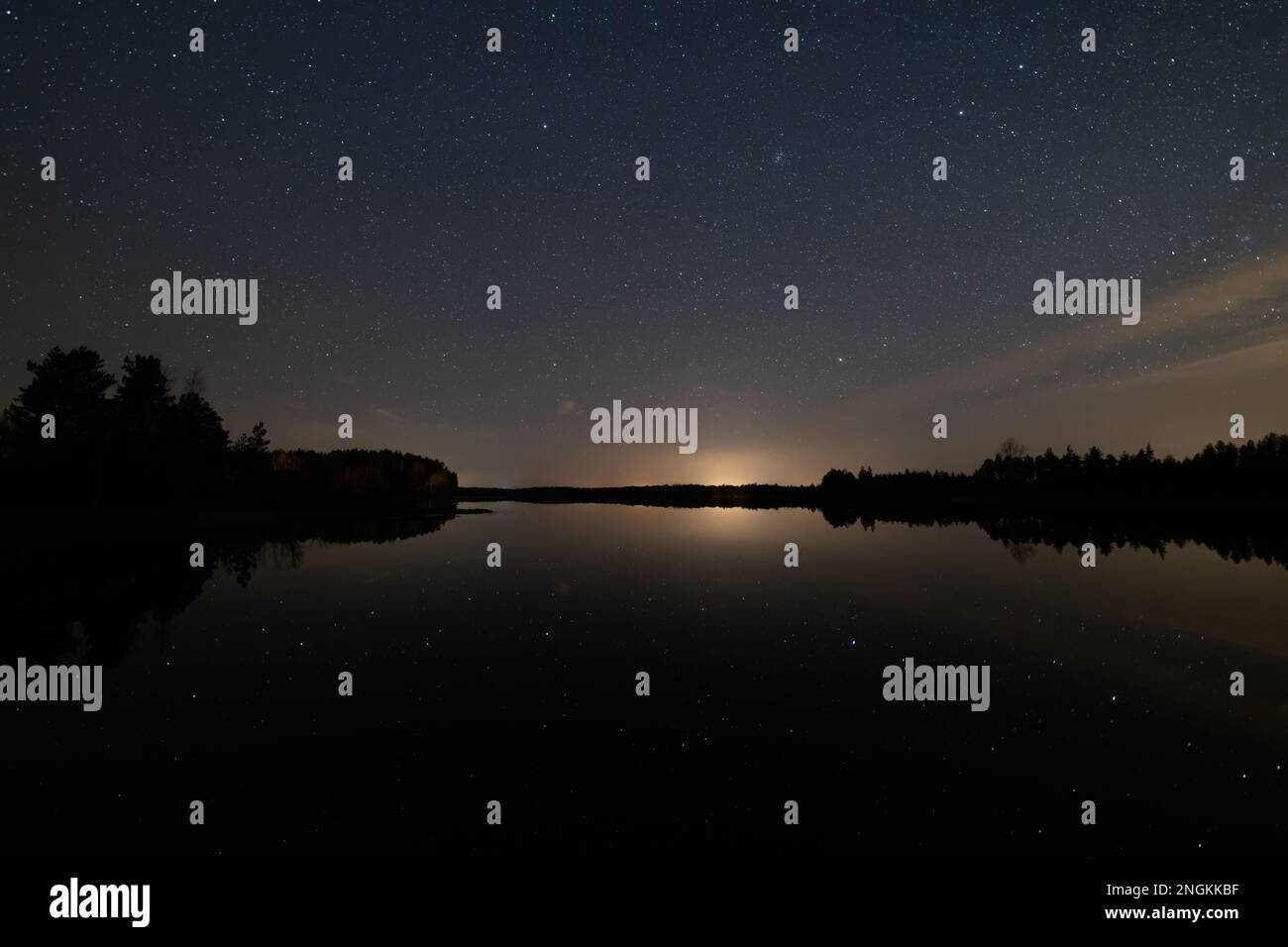 Starry night sky over a wild lake with stars reflecting in the still ...