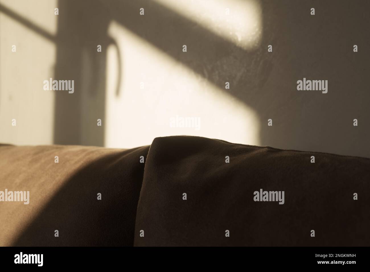 indoor shot of a couch with window frame shadow on it and on the wall ...