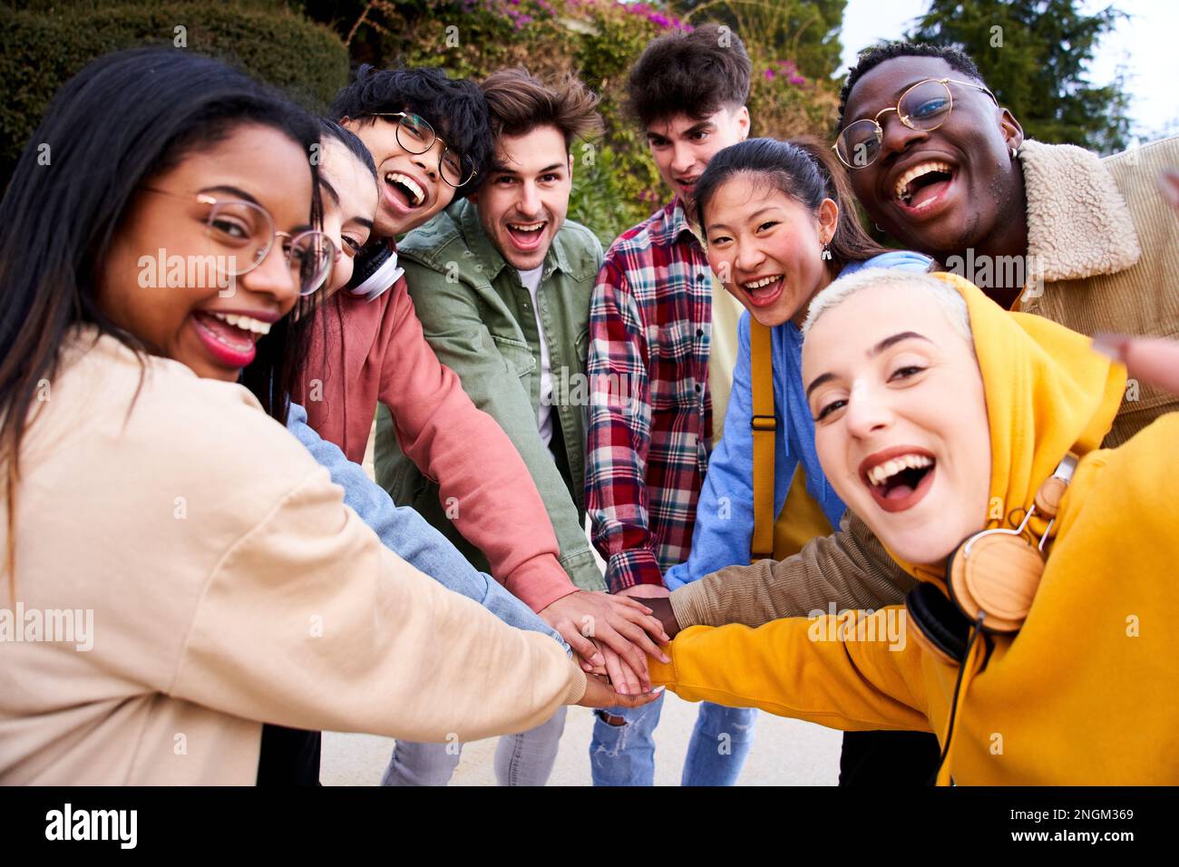 Cheerful multiracial group of students making pile hands and smiling at ...