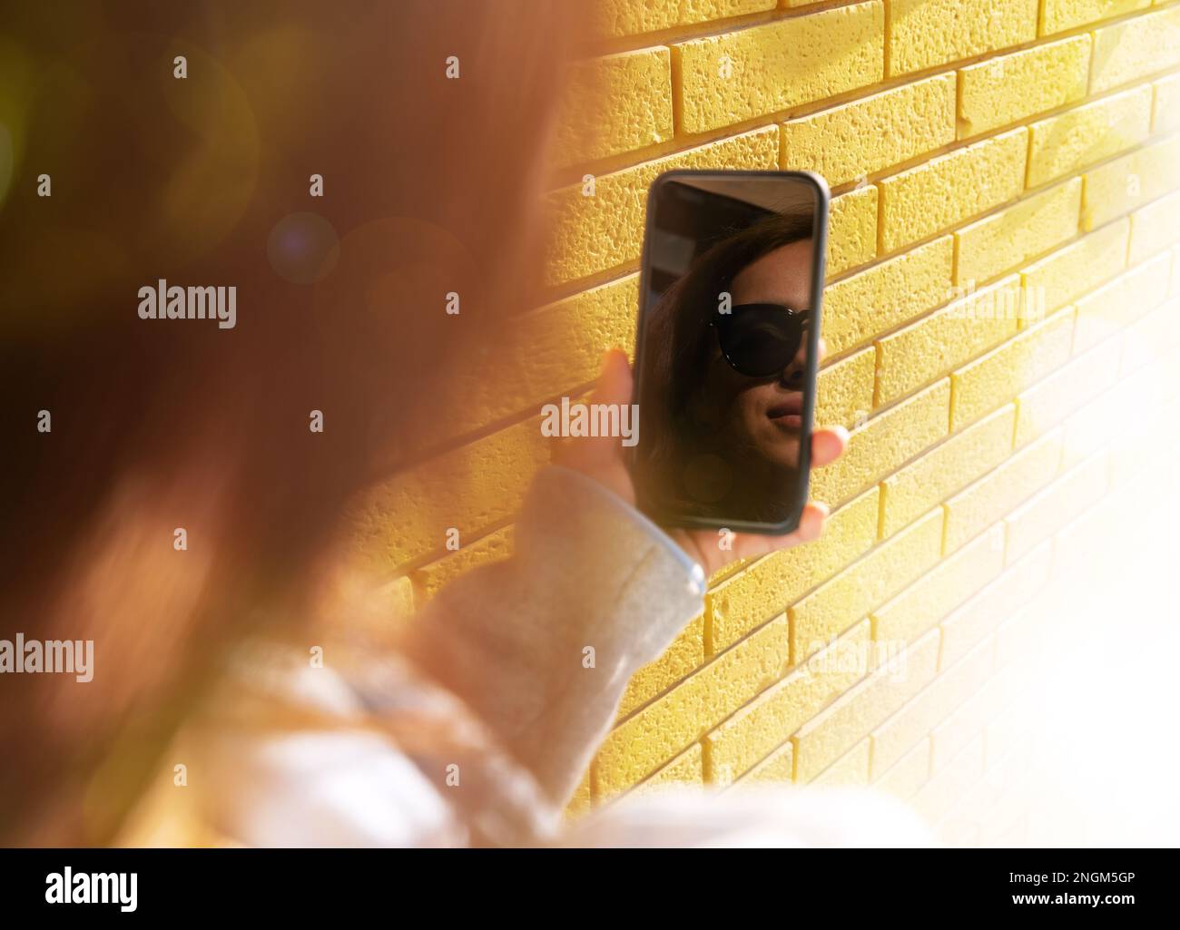 Woman face reflection in screen of mobile phone against brick wall ...