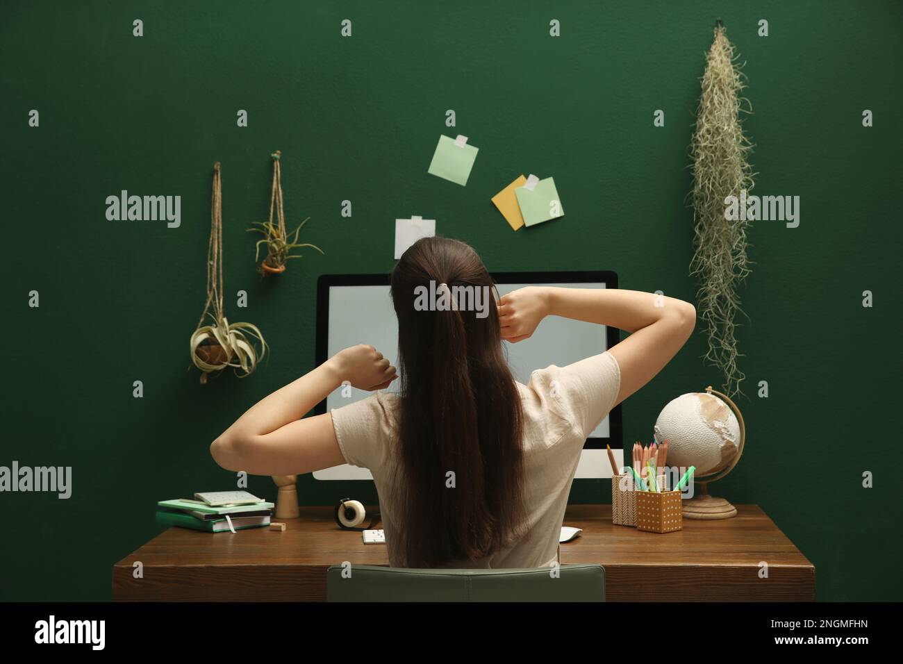 Woman sitting at wooden desk with computer near green wall, back view ...