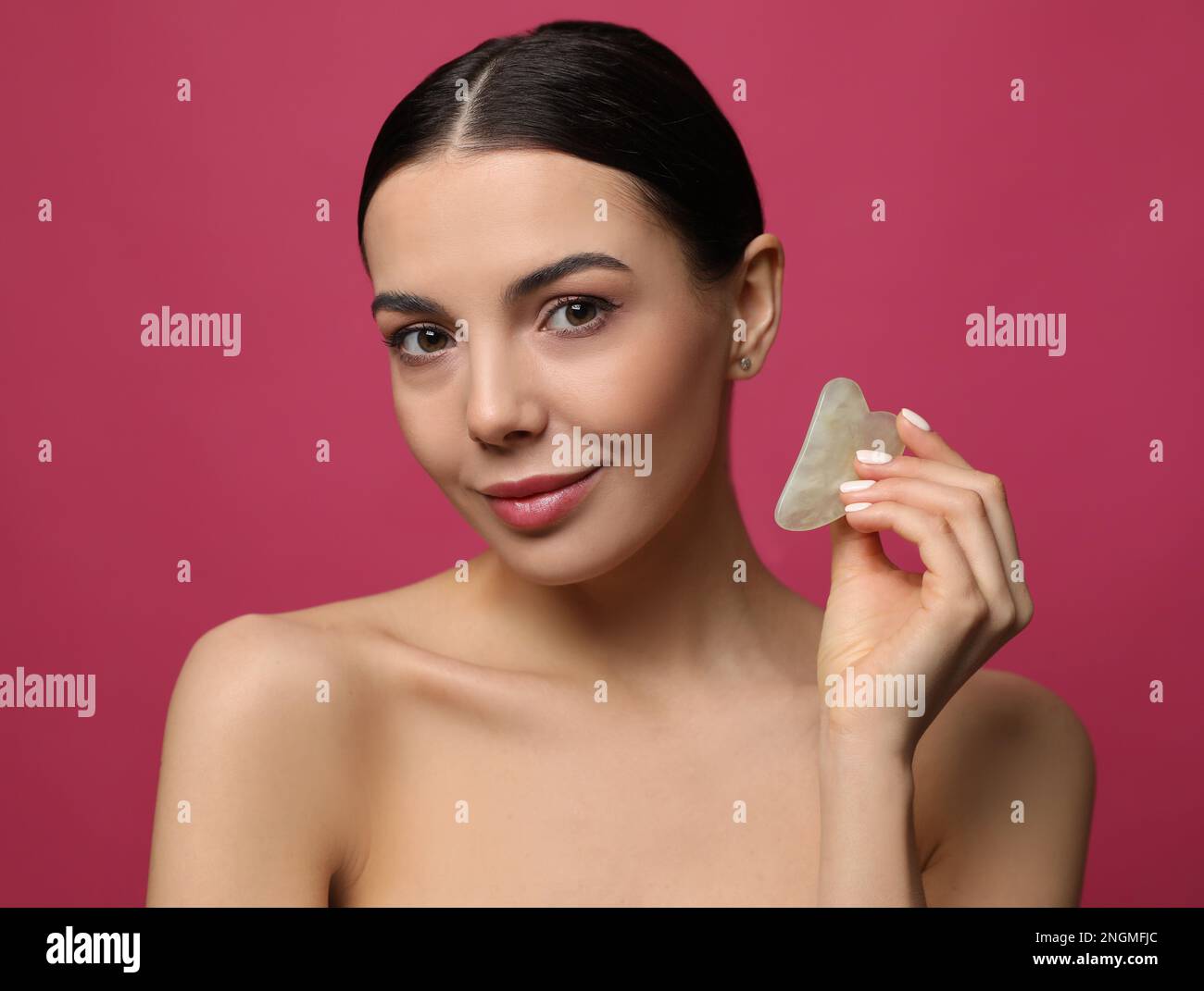 Beautiful young woman doing facial massage with gua sha tool on pink background Stock Photo - Alamy