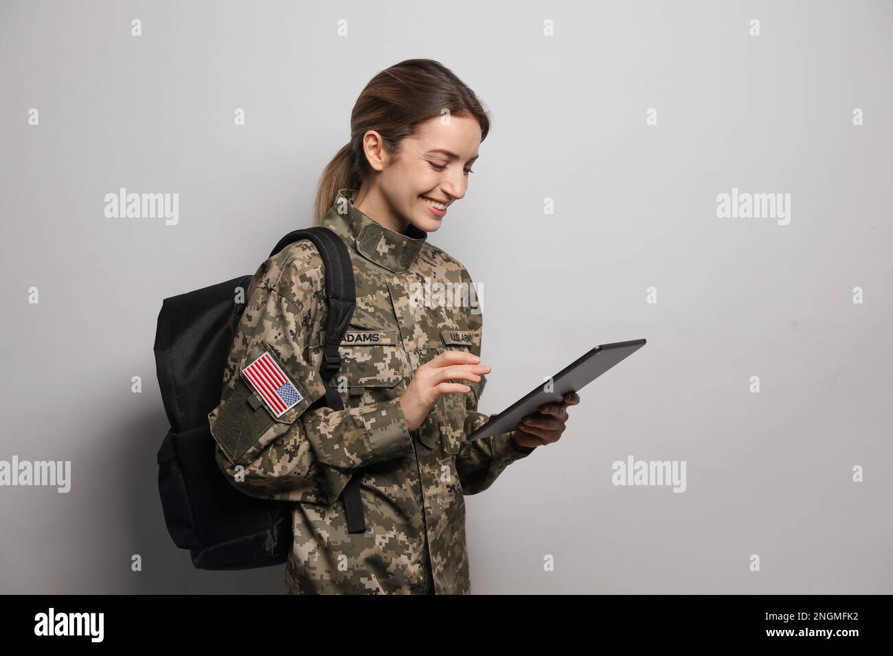 Female cadet with backpack and tablet on light grey background ...