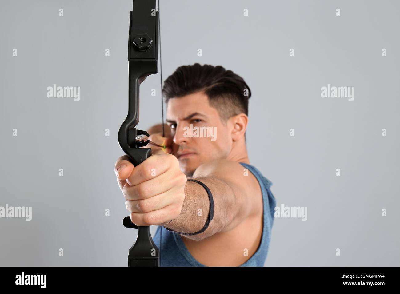 Man with bow and arrow practicing archery against light grey background ...