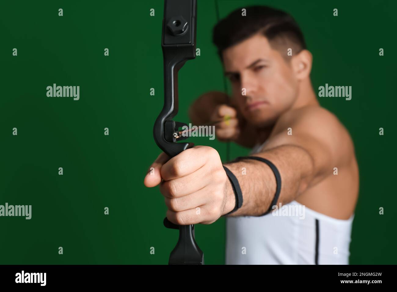 Man with bow and arrow practicing archery against green background ...