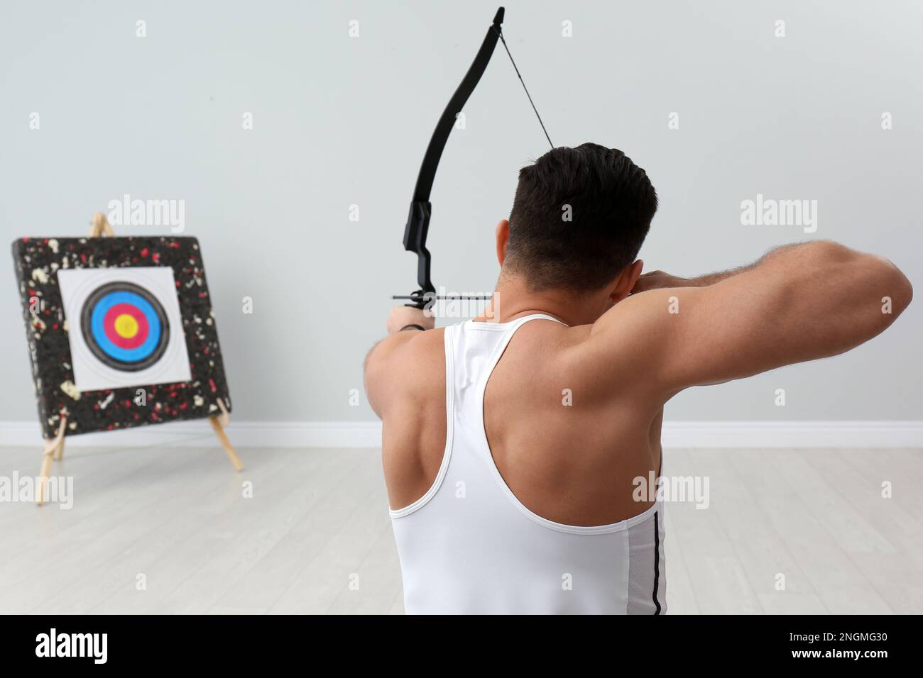Man with bow and arrow aiming at archery target indoors Stock Photo - Alamy