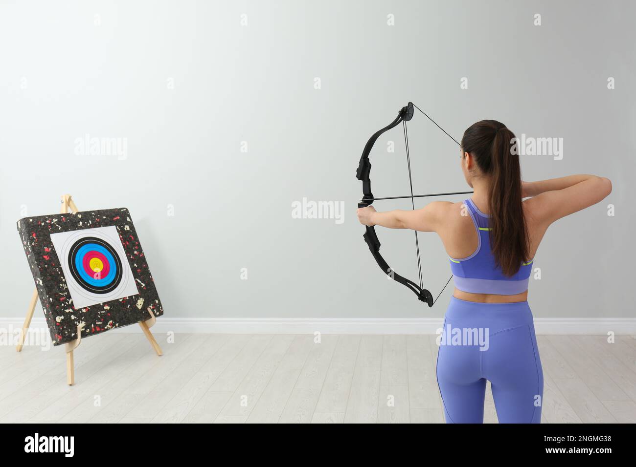 Woman with bow and arrow aiming at archery target indoors, back view ...