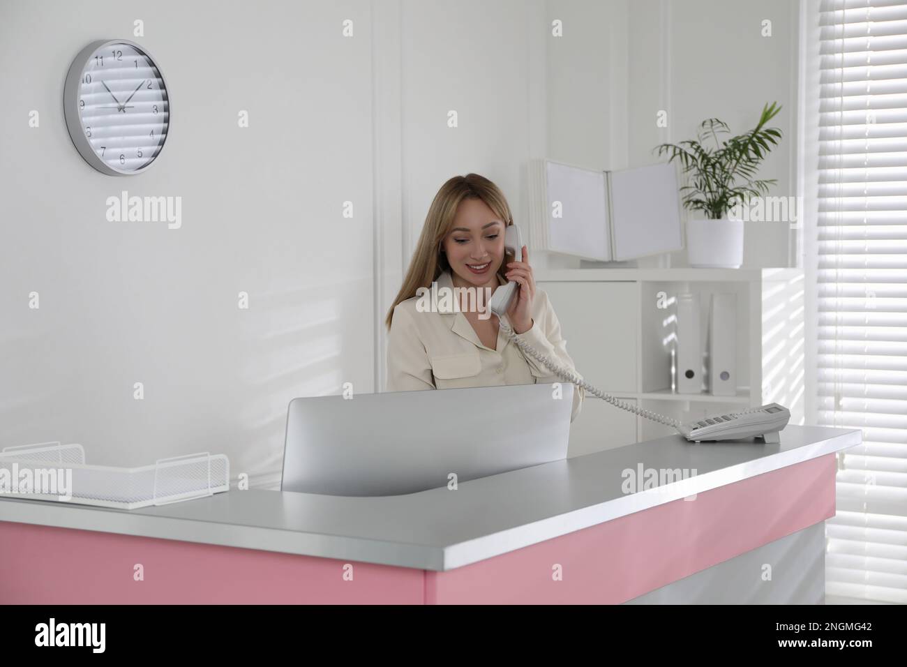 Receptionist talking on phone at countertop in office Stock Photo - Alamy