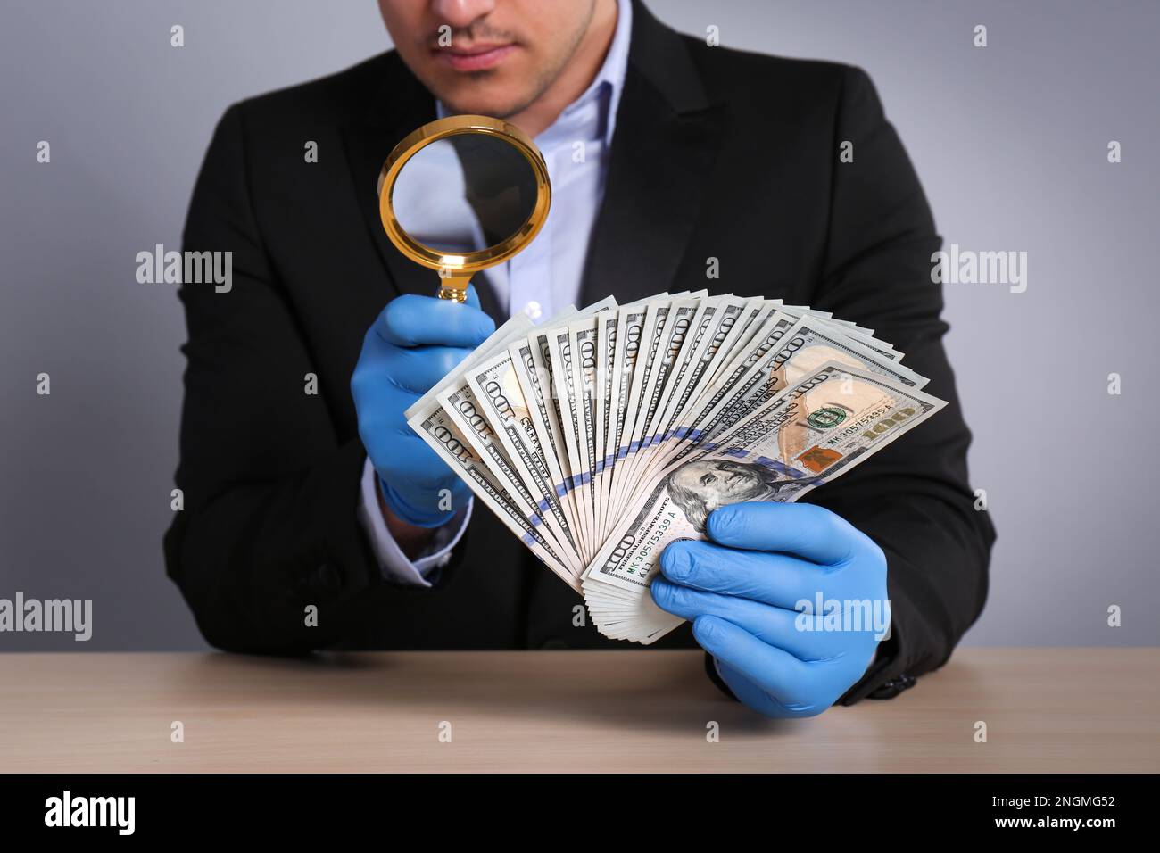 Expert authenticating 100 dollar banknotes with magnifying glass at ...