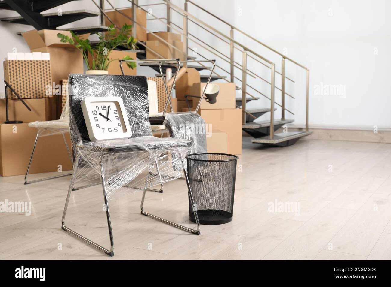 Packed chair, trash bin and clock near stairs in office, space for text ...