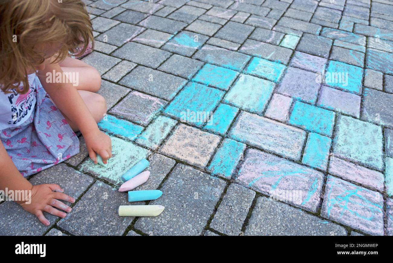 Child paints with colorful chalk on concrete pavement Stock Photo - Alamy