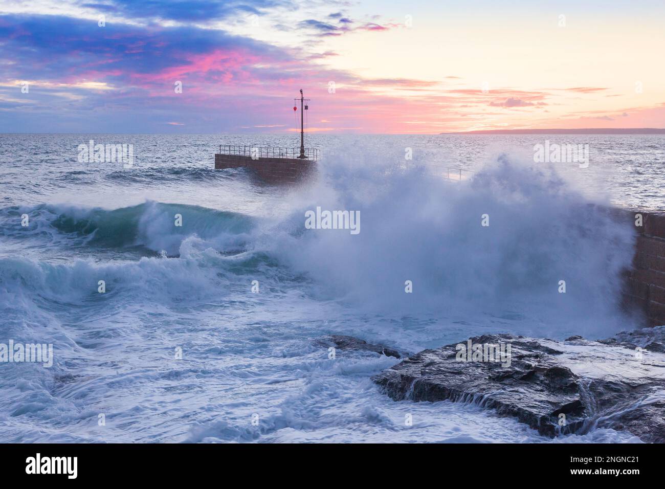 Spring tide waves splash over Porthleven Pier during a colourful sunset ...