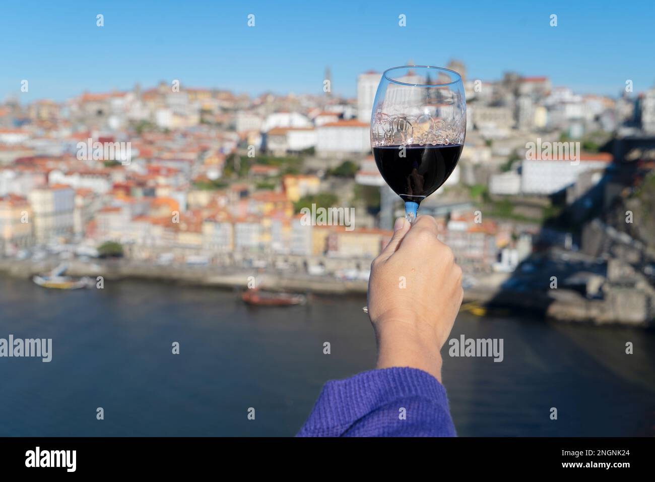 hand of woman with glass of ruby port wine on historic town of Porto ...