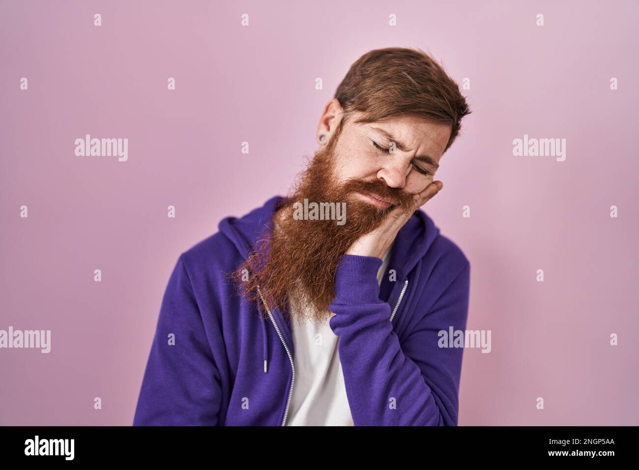Caucasian man with long beard standing over pink background thinking ...