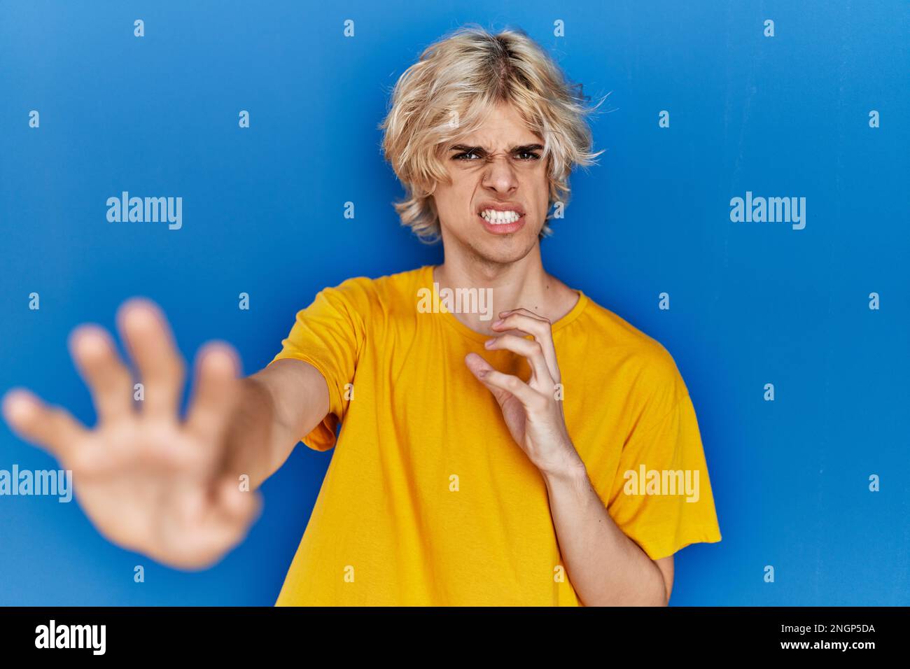 Young modern man standing over blue background disgusted expression ...