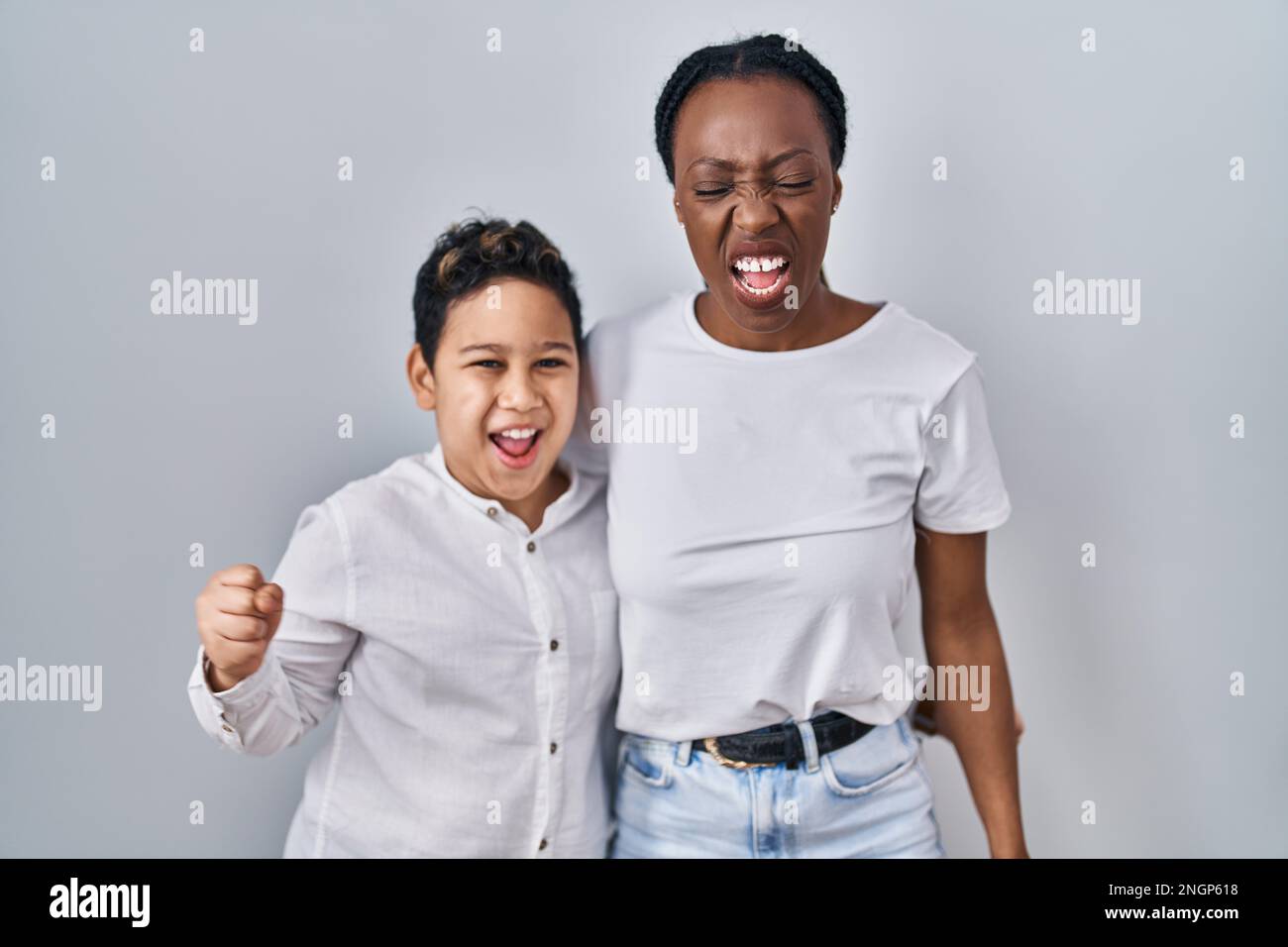 Young mother and son standing together over white background angry and ...