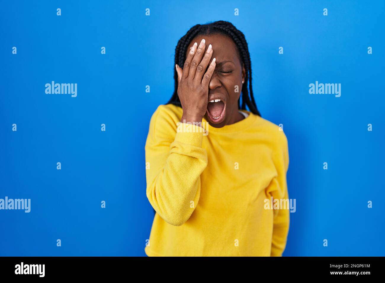 Beautiful black woman standing over blue background yawning tired ...