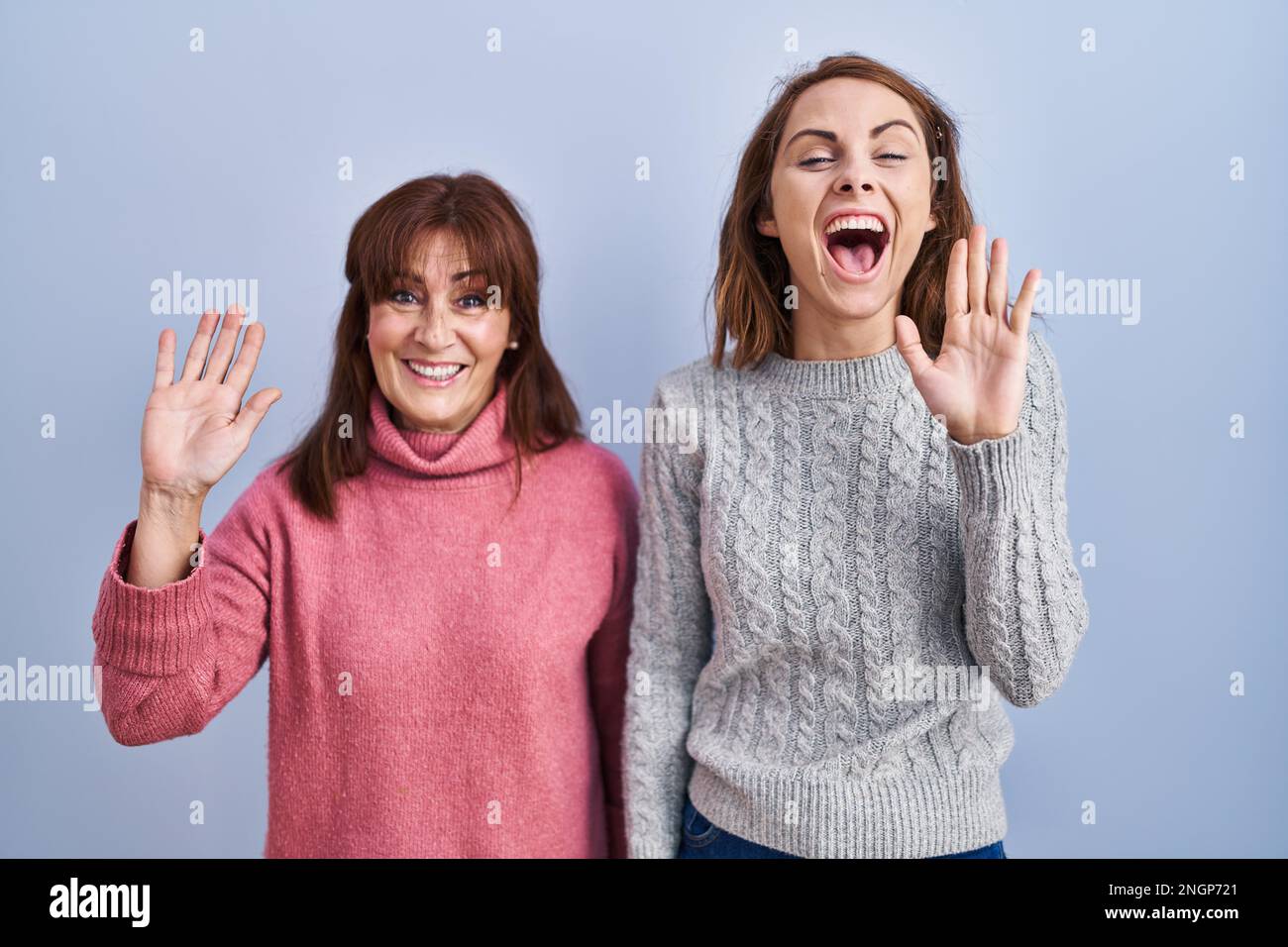 Mother And Daughter Standing Over Blue Background Waiving Saying Hello