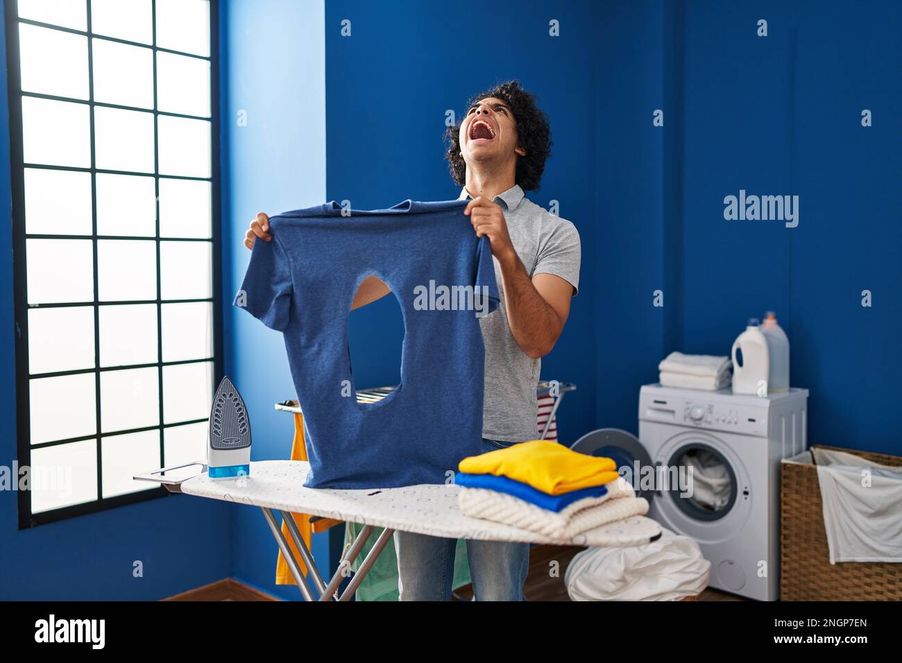 Hispanic man with curly hair ironing holding burned iron shirt at ...