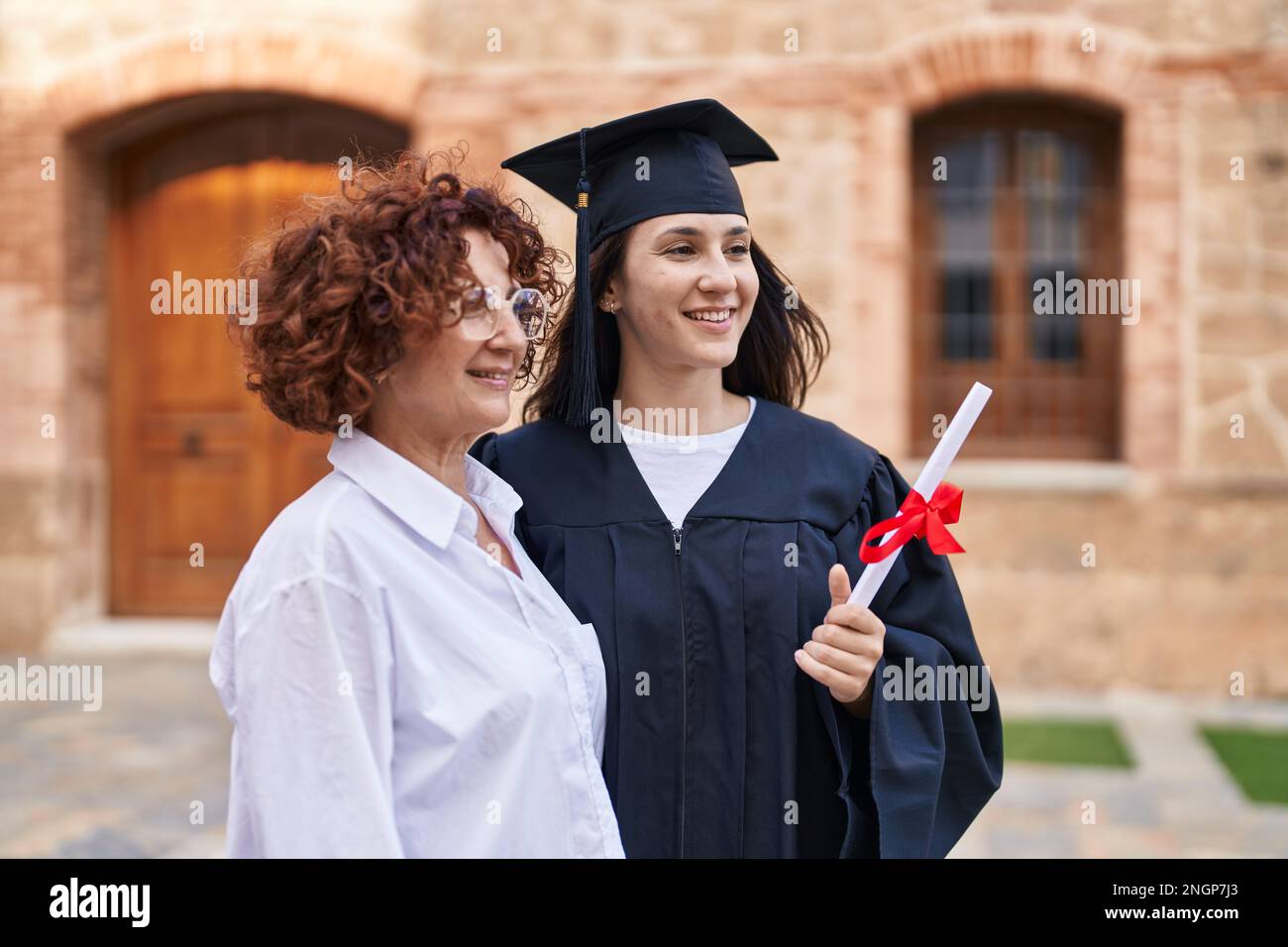 Two women mother and daughter holding graduate diploma at campus ...