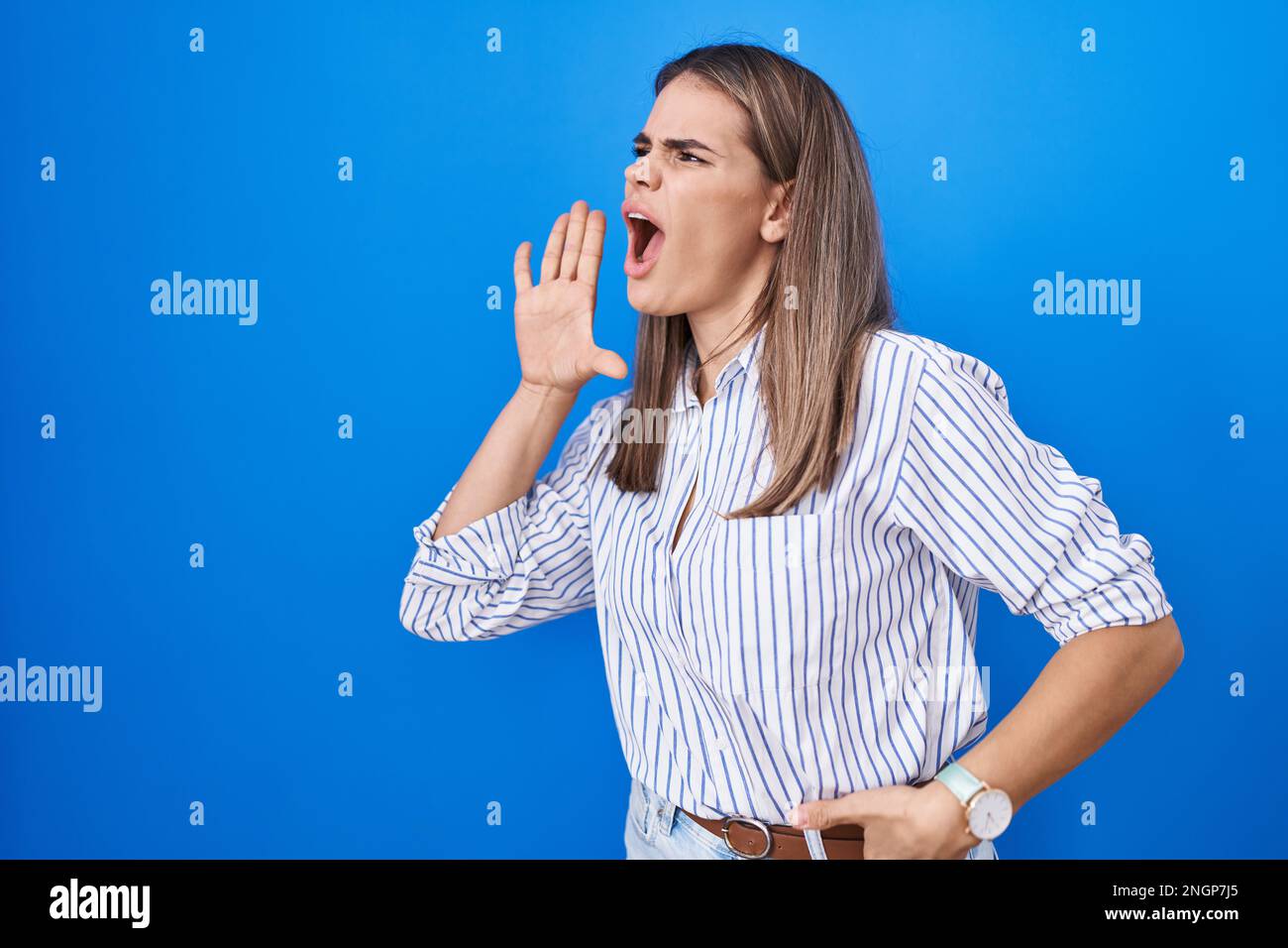 Hispanic young woman standing over blue background shouting and ...