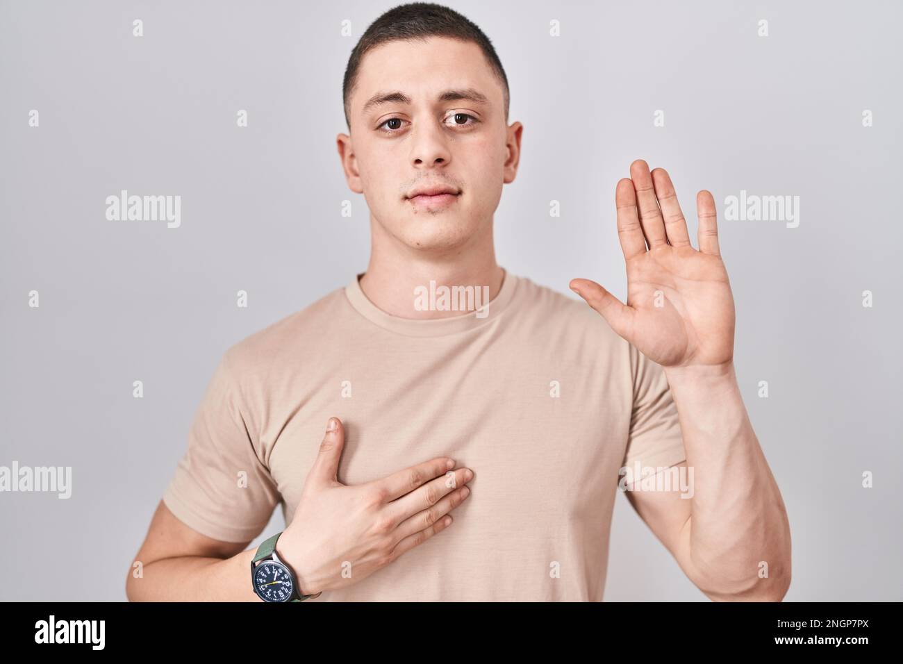Young man standing over isolated background swearing with hand on chest ...