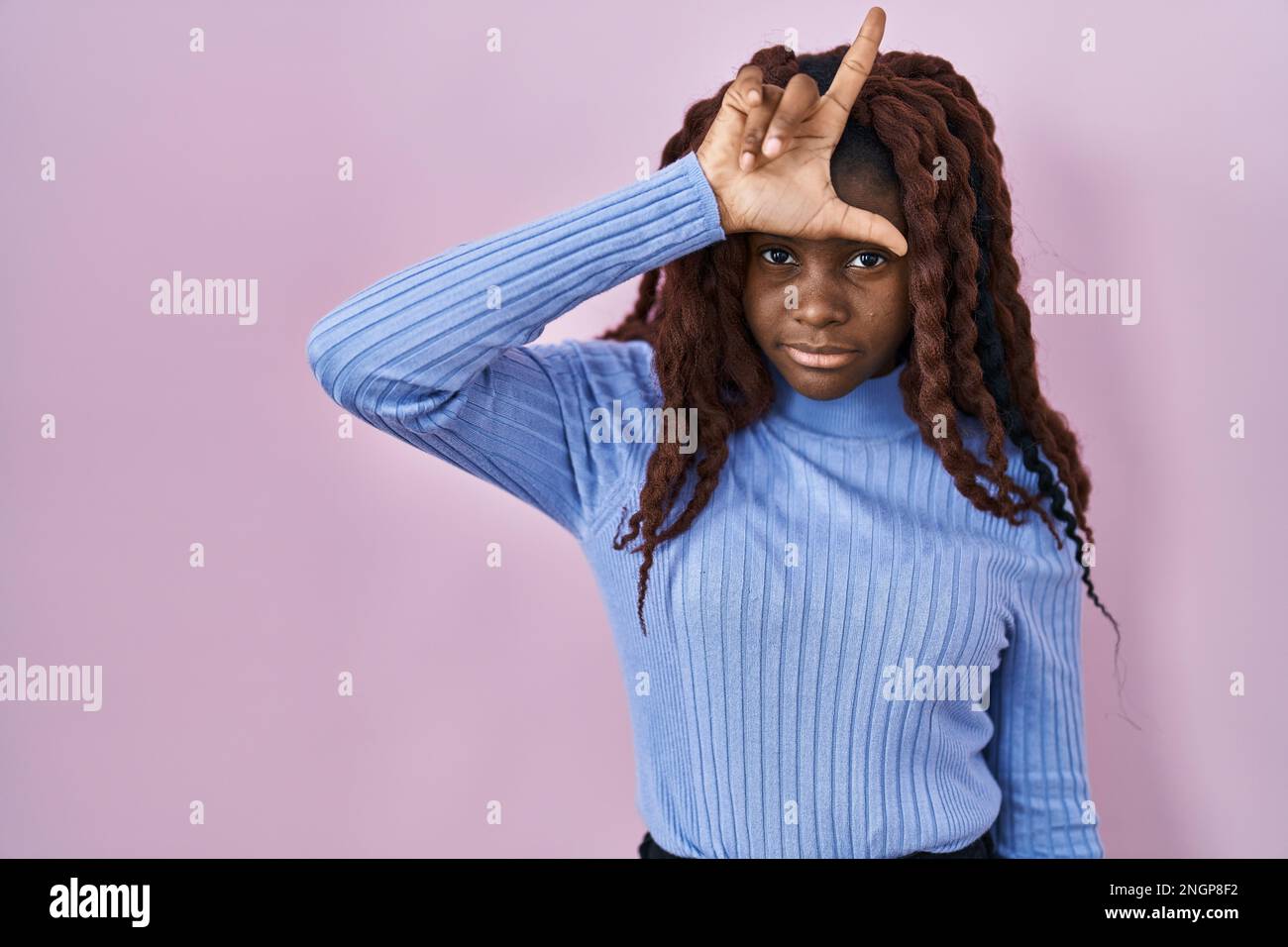 African woman standing over pink background making fun of people with ...