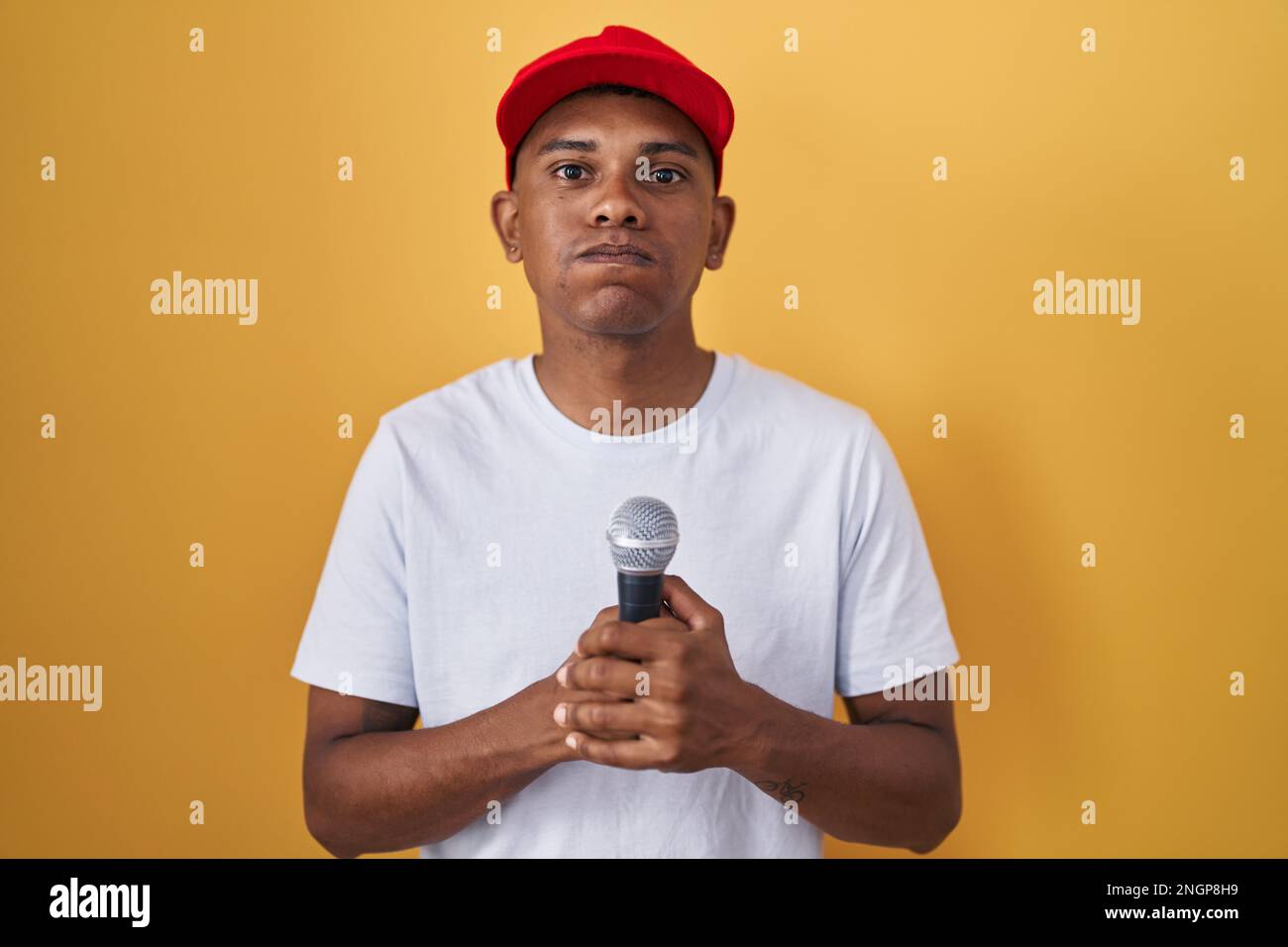 Young hispanic man singing song using microphone puffing cheeks with ...