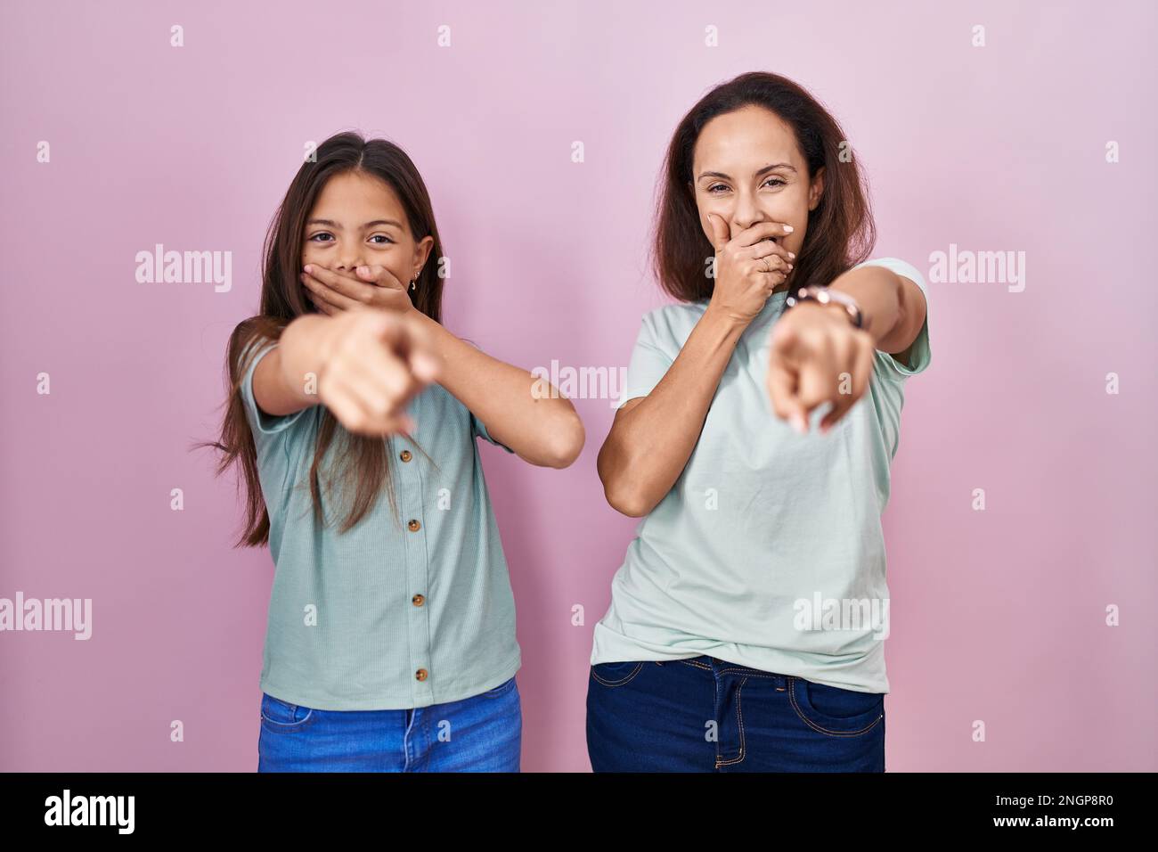Young mother and daughter standing over pink background laughing at you ...
